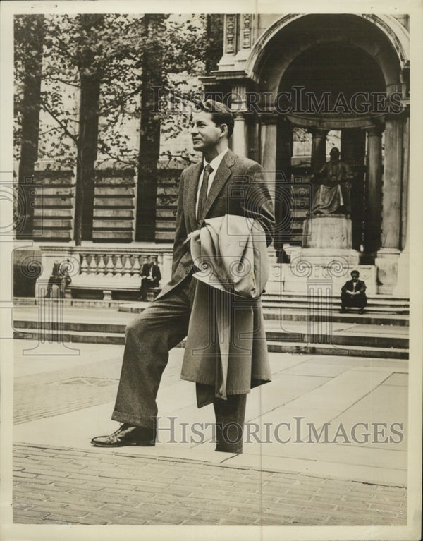 Undated Ralph Lowe holding a coat and standing in front of stone statue ...