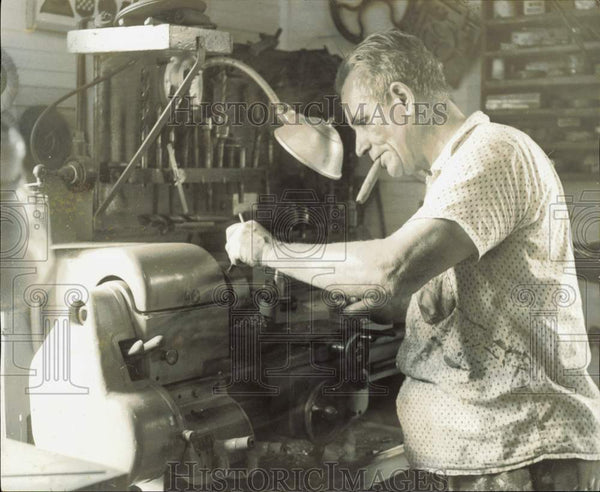 1959 Press Photo James L. Logan smokes a cigar and works on a machine ...